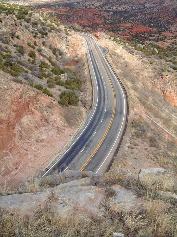 Colorful canyon walls embrace this serpentine road that twists through layers of ancient rock like a ribbon through time.