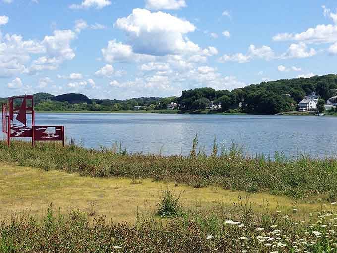 Wildflowers and grasses frame the peaceful river view where sailboats drift lazily in the distance.