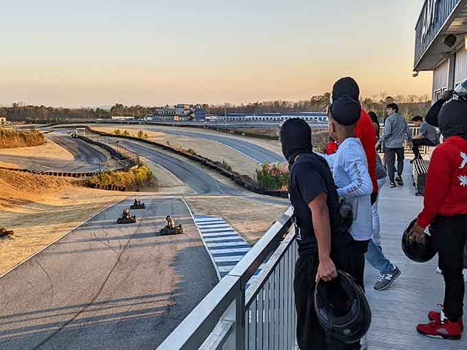 Spectators gather at golden hour, helmets in hand, anticipation building as they watch the action unfold below them.