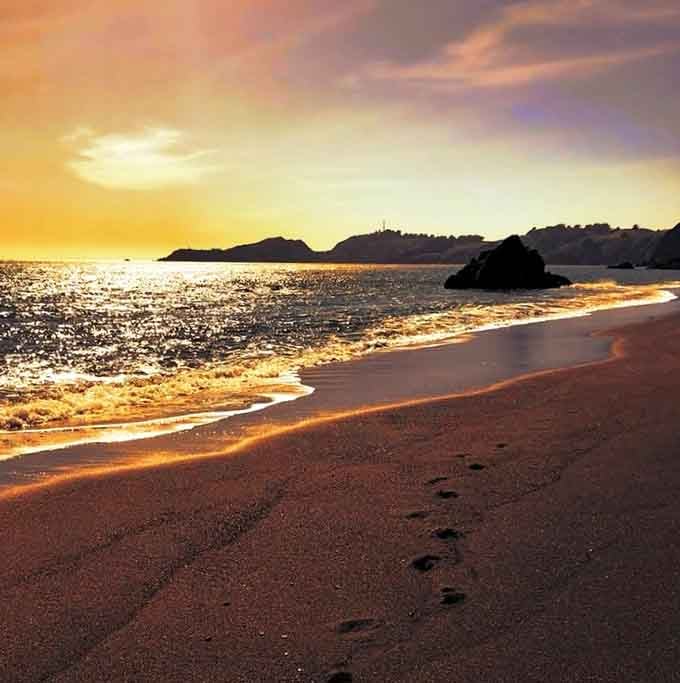 Golden hour transforms black sand into bronze, proving this beach has more costume changes than Cher.