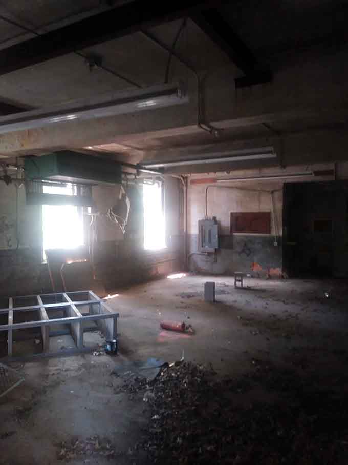 Sunlight pierces the gloom of this gutted space, revealing exposed pipes and forgotten industrial remnants.