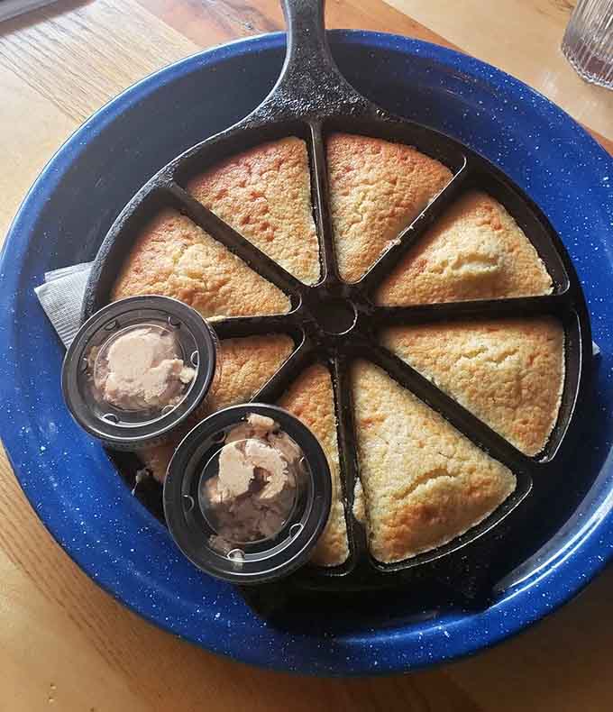 Cornbread wedges served in a cast-iron skillet, because some camping traditions are absolutely worth keeping indoors.