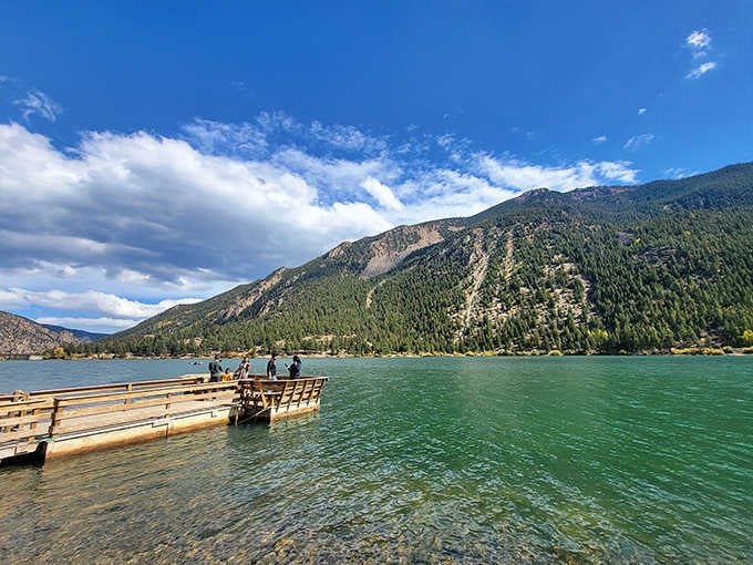 That dock stretches into water so clear you can practically see tomorrow, with mountains reflected like nature's own mirror.