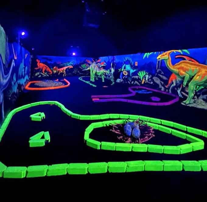 Glowing pathways wind through darkness like ancient jungle trails, each turn revealing another fluorescent dinosaur standing sentinel over your putt.