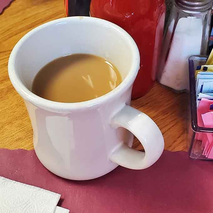Simple white mug filled with hot coffee that gets refilled before you even realize you need it, pure diner magic.