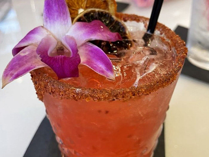 A cocktail garnished with an actual orchid, because apparently your beverage deserves to feel fancy and tropical too.