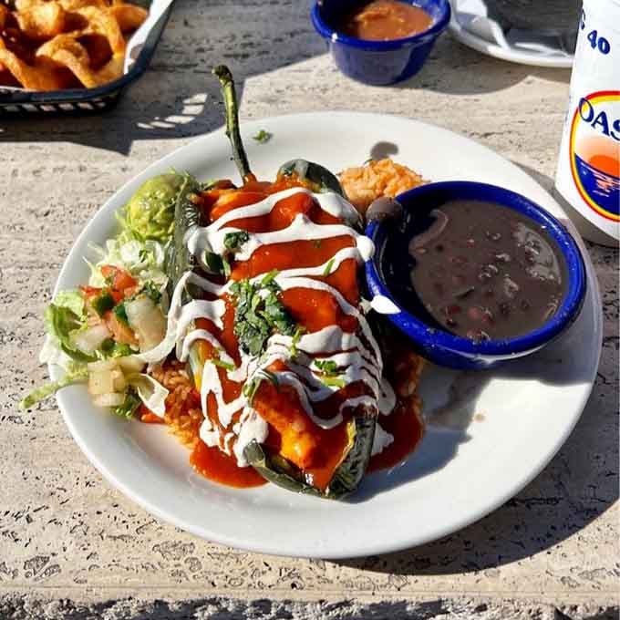 A stuffed poblano pepper dressed in red sauce and sour cream, sitting next to rice and beans like royalty.