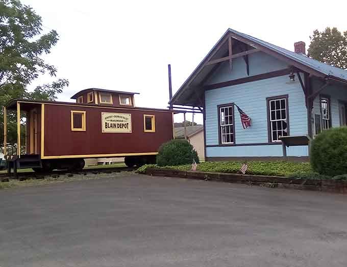 A vintage caboose sits beside a modest station building, preserving railroad heritage in the most charming and accessible way possible.