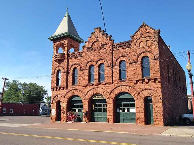This sandstone fire station stands like a fortress of civic pride, its Romanesque arches framing doors that once protected the community.