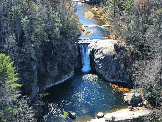 From this bird's-eye view, the waterfall plunges dramatically into a sapphire pool surrounded by rocky cliffs and forest.