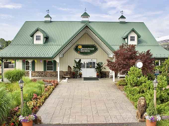 The green-roofed barn building beckons visitors down a paver path flanked by colorful flowers and welcoming lamp posts.