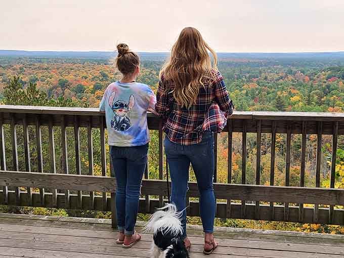 Two generations stand together, gazing at fall's spectacular color show stretching endlessly toward the horizon below.