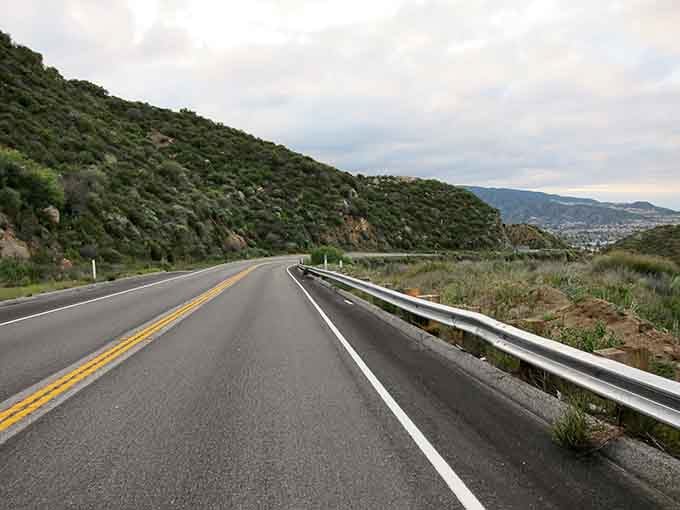 Sage-covered hillsides stretch toward the horizon as the road cuts through classic California backcountry landscape.