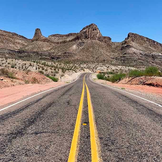 Jagged rock formations stand guard over this desert highway where the yellow line points straight toward geological wonders ahead.