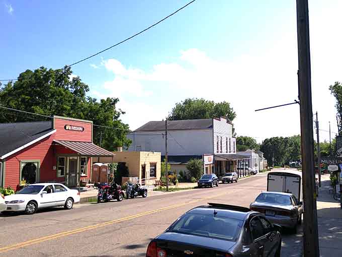 This quiet main street stretches toward endless possibilities where motorcycles park beside cars without any fuss.