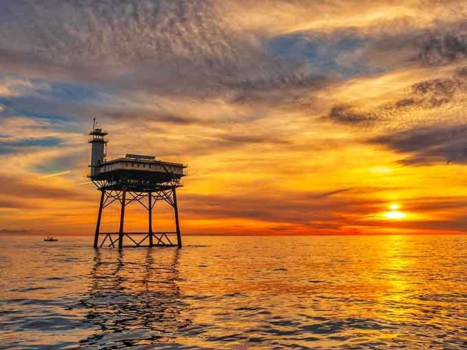 Golden hour transforms this offshore sentinel into a silhouette against clouds that look hand-painted across the evening sky.