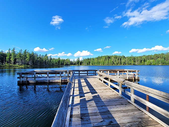 Weathered dock stretches toward crystal-blue water under endless sky, inviting contemplation and maybe some serious daydreaming too.