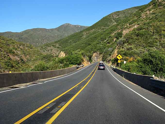Lush green mountains embrace the highway, creating a tunnel of nature that feels refreshingly cool and peaceful.