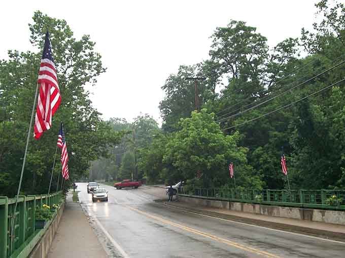 Rain-slicked pavement reflects the green bridge and patriotic banners, adding moody beauty to this valley town's entrance.
