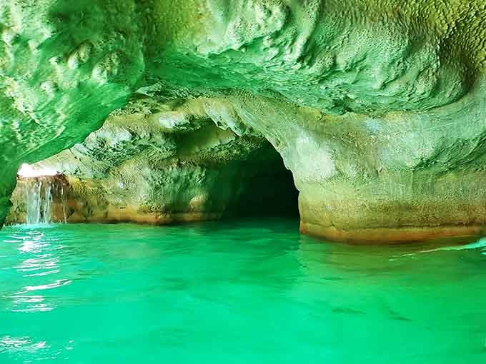 Emerald water glows beneath natural rock formations, creating a secret grotto that feels like discovering hidden treasure.