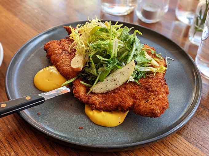 The Milanese arrives golden and crispy, topped with fresh greens that add the perfect bright counterpoint to richness.