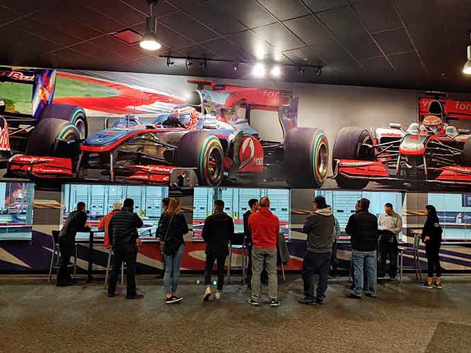 Spectators watching beneath Formula One cars, living vicariously through racers while their own hearts recover from earlier.