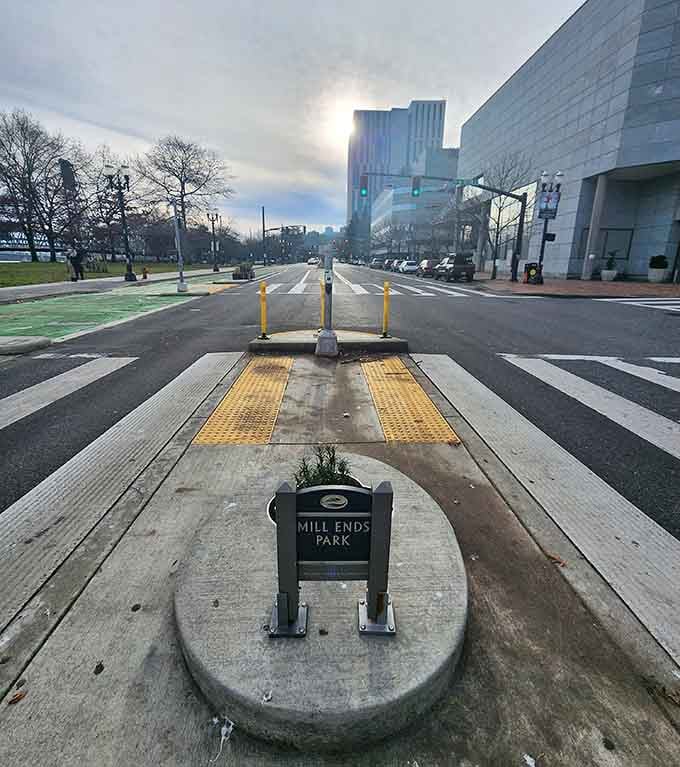 Yellow crosswalk markings lead visitors safely to this median marvel, because even tiny parks deserve proper pedestrian access and respect.