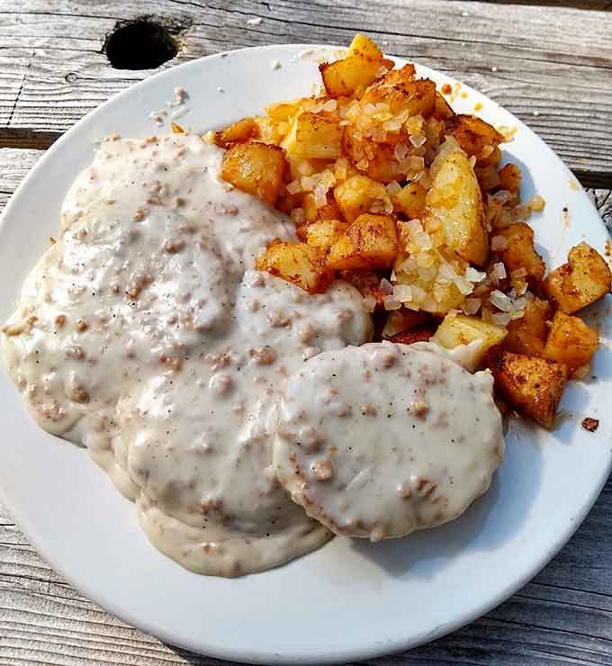 Creamy sausage gravy blanketing biscuits with golden homefries is comfort food that hugs you from the inside out.