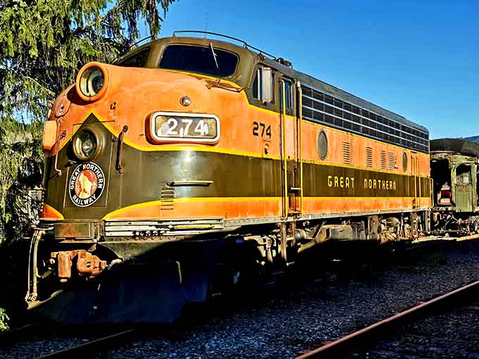 The Great Northern Railway's orange and yellow diesel engine gleams in the sunlight, a colorful piece of railroad heritage.