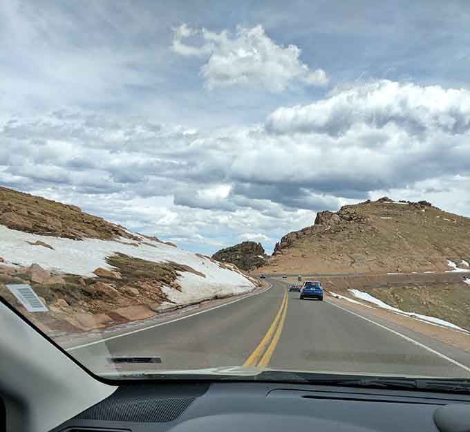 Follow the road as it stretches toward the horizon, surrounded by vast evergreen forests and the stunning peaks of Colorado.