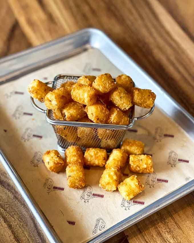 Golden, crispy Tater Tots at Sandwichitos arrive like tiny pillows of happiness begging for cheese sauce baptism.