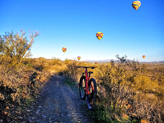 Hot air balloons drift overhead like colorful dreams, adding whimsy to your morning ride through this desert wonderland.