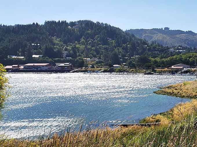 The harbor sparkles under blue skies, where a calm river winds through and forested hills create a backdrop worthy of a movie set.