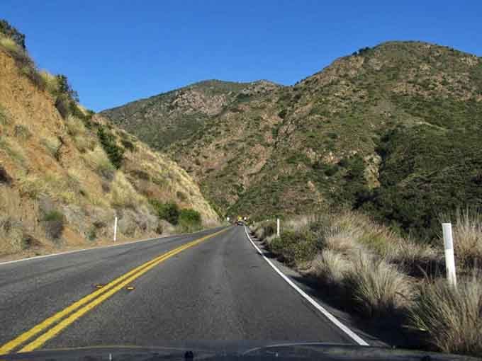 Mountains rise on both sides of this valley road, standing guard like ancient sentinels watching over your journey.