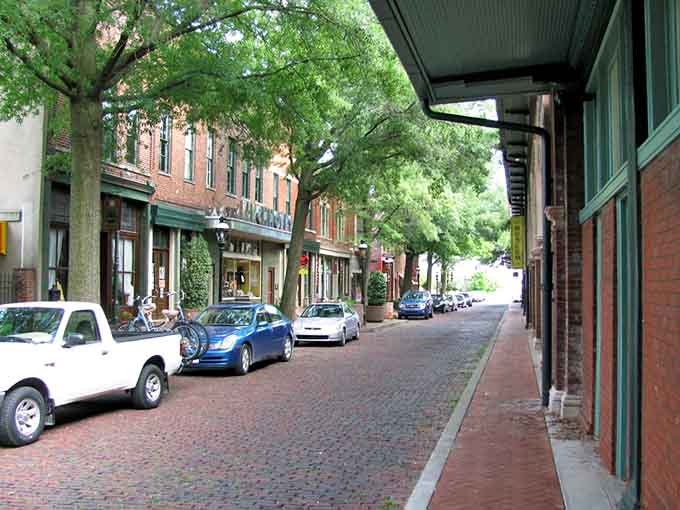 Brick sidewalks and leafy canopies create natural air conditioning, making window shopping feel like a leisurely stroll through living history.