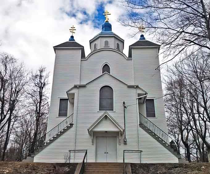 This pristine white church with triple domes rises majestically through bare trees, looking like something transported straight from Eastern Europe.