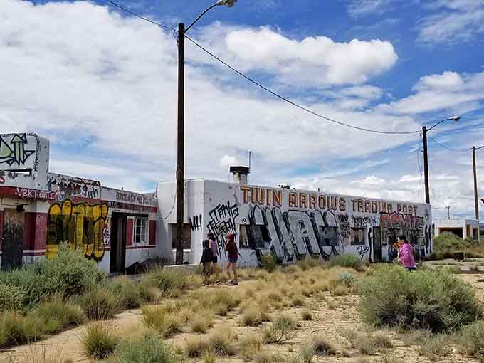 Desert vegetation reclaims the old trading post while visitors explore the graffiti-covered walls, experiencing this unique blend of history and urban art.