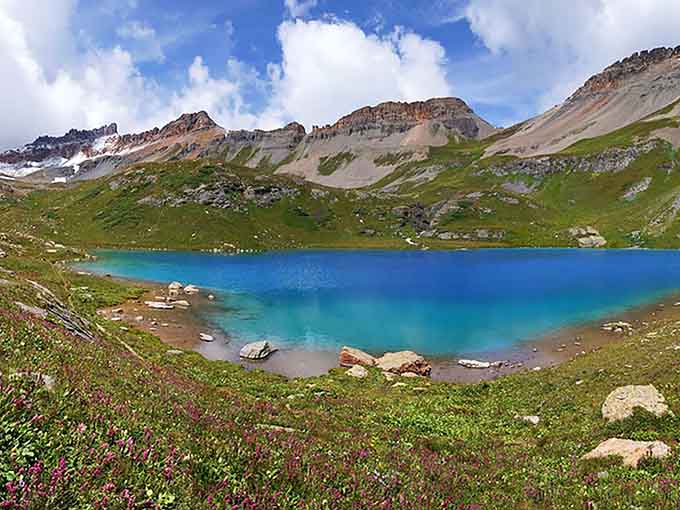 That electric blue shoreline framed by wildflowers and jagged peaks is nature showing off without apology.