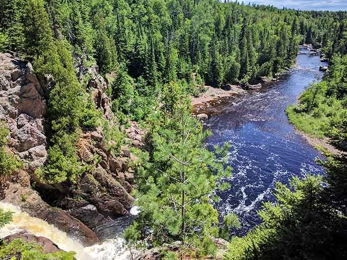 Ancient volcanic cliffs drop dramatically into the rushing Baptism River, framed by a sea of deep green North Shore forest.