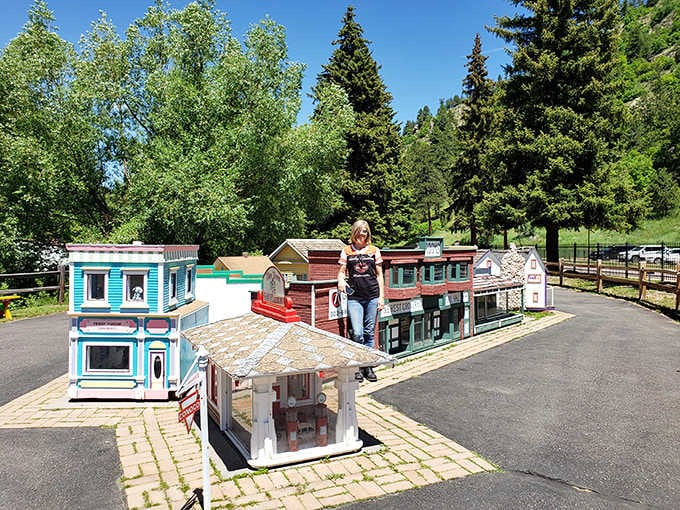 A woman stands among colorful miniature storefronts while towering Colorado pines frame this one-of-a-kind mountain village perfectly.