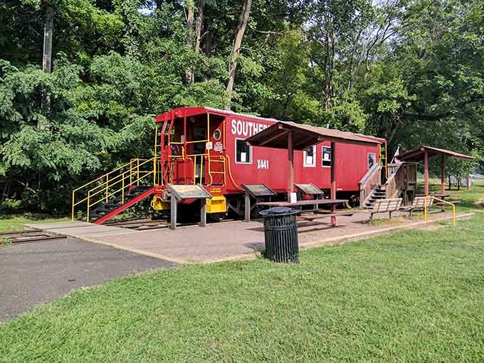 A bright red caboose sitting in an open green field, quietly daring you to walk on past.
