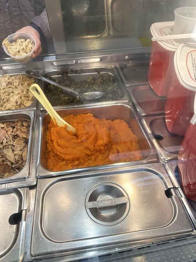 That vibrant sweet potato sitting next to dark, tender collard greens is soul food poetry served in a steam tray.