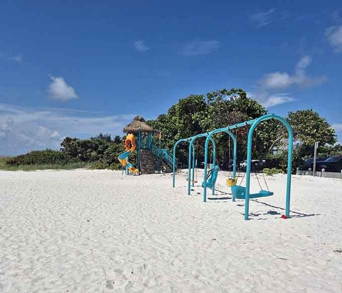 Teal swings, a thatched-roof play structure, and sand so soft it doubles as a landing pad. This beach playground wins every single time.