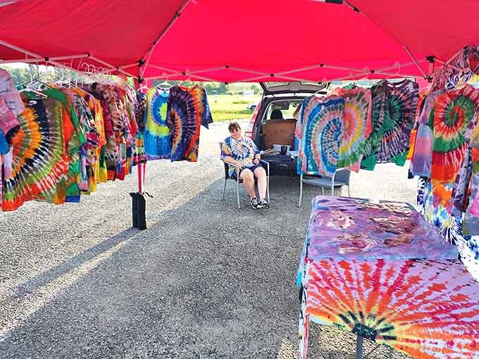 A rainbow of tie-dye hanging under a red canopy, loud, joyful, and completely impossible to walk past without smiling.