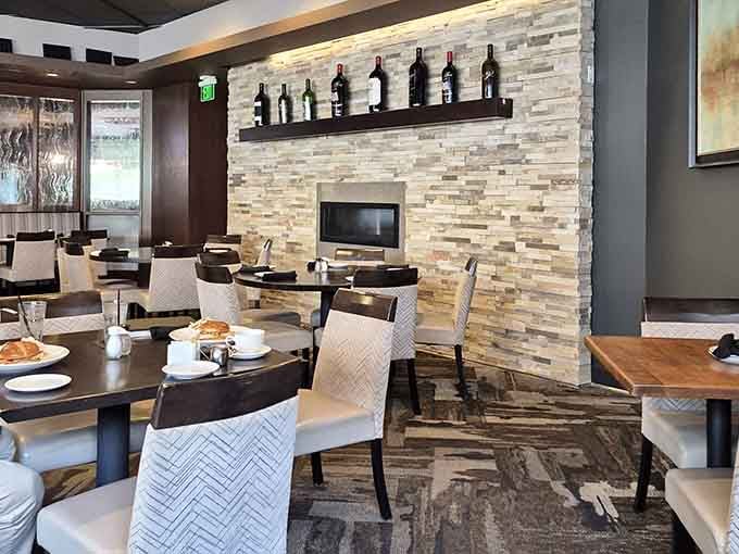 A stacked stone fireplace, wine bottles on the shelf, and comfortable chairs. This dining room earns its cozy reputation.