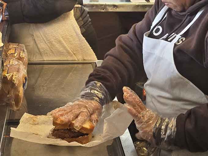 Gloved hands building a sandwich with quiet confidence. This is the kind of craftsmanship that no culinary school can fully teach you.