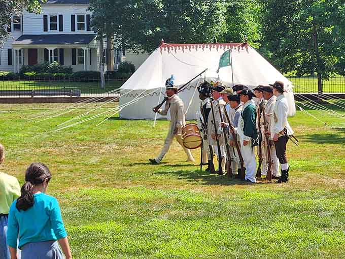 Reenactors line up in formation while kids watch, proving history class is better with drums and muskets.
