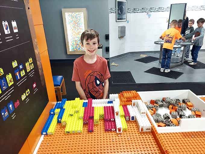 That grinning kid in the Spider-Man shirt just built something magnificent at the Lego station, and his expression says absolutely everything.