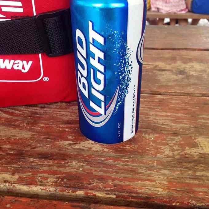 A cold Bud Light on a worn wooden table, the simplest possible companion to world-class smoked meat on a sunny afternoon.