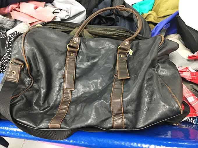 A well-traveled leather duffle bag with decades of character, sitting in a bin and quietly hoping someone appreciates the journey.